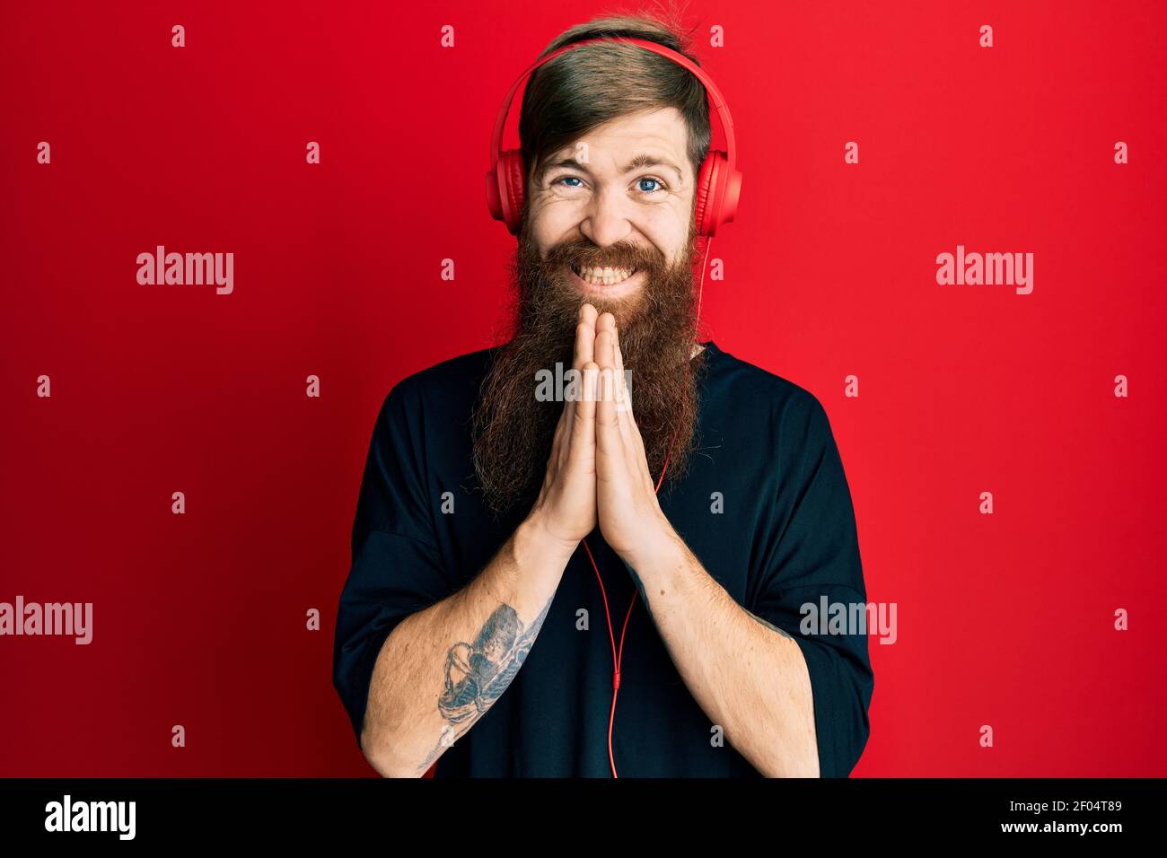 Redhead man with long beard listening to music using headphones praying ...