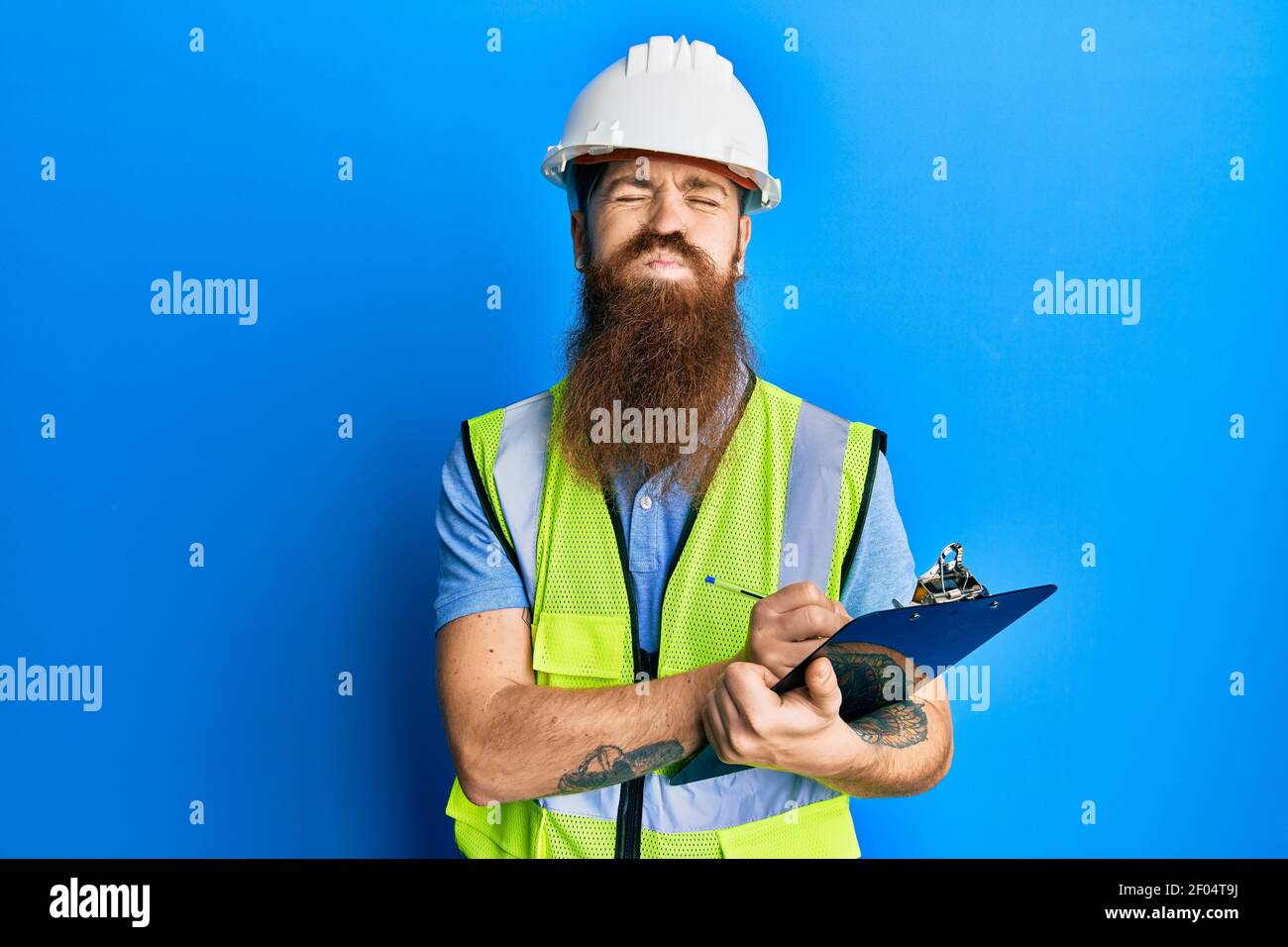 Redhead man with long beard wearing safety helmet holding clipboard ...