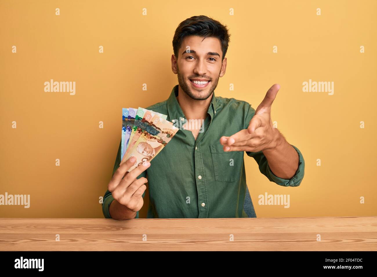 Young handsome man holding canadian dollars smiling friendly offering ...