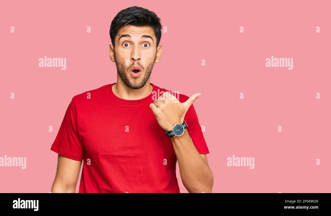 Young handsome man wearing casual red tshirt surprised pointing with ...