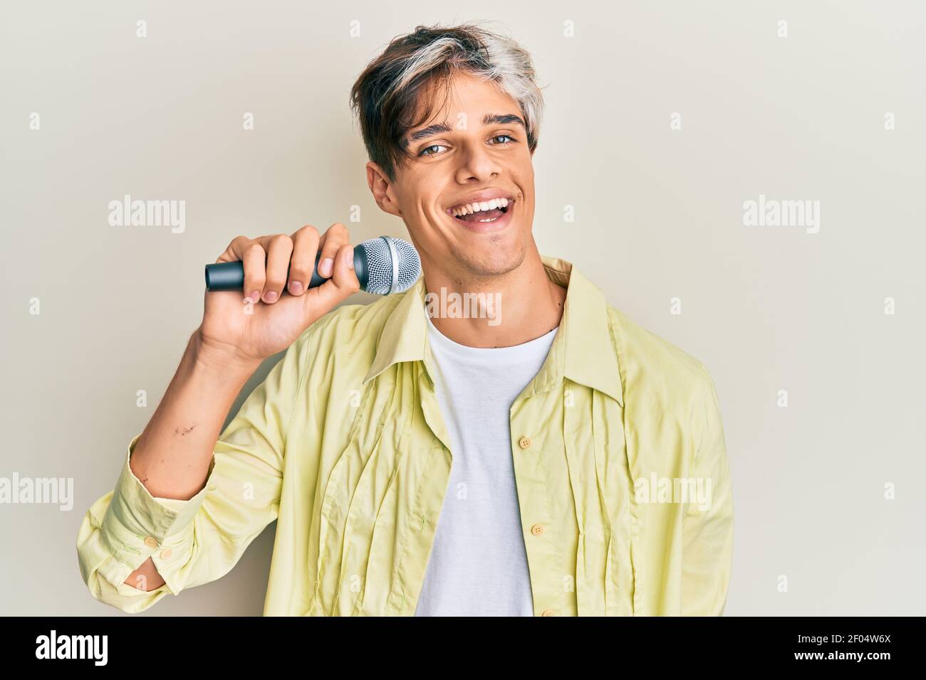 Young hispanic man singing song using microphone looking positive and ...