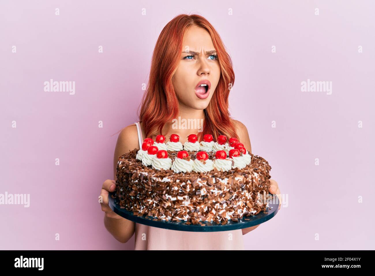 Young redhead woman celebrating birthday with cake angry and mad ...