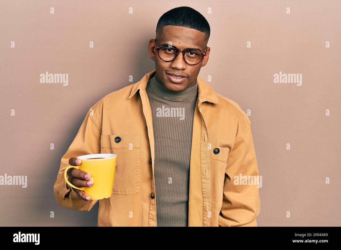 Young black man wearing glasses and drinking a cup of coffee looking ...