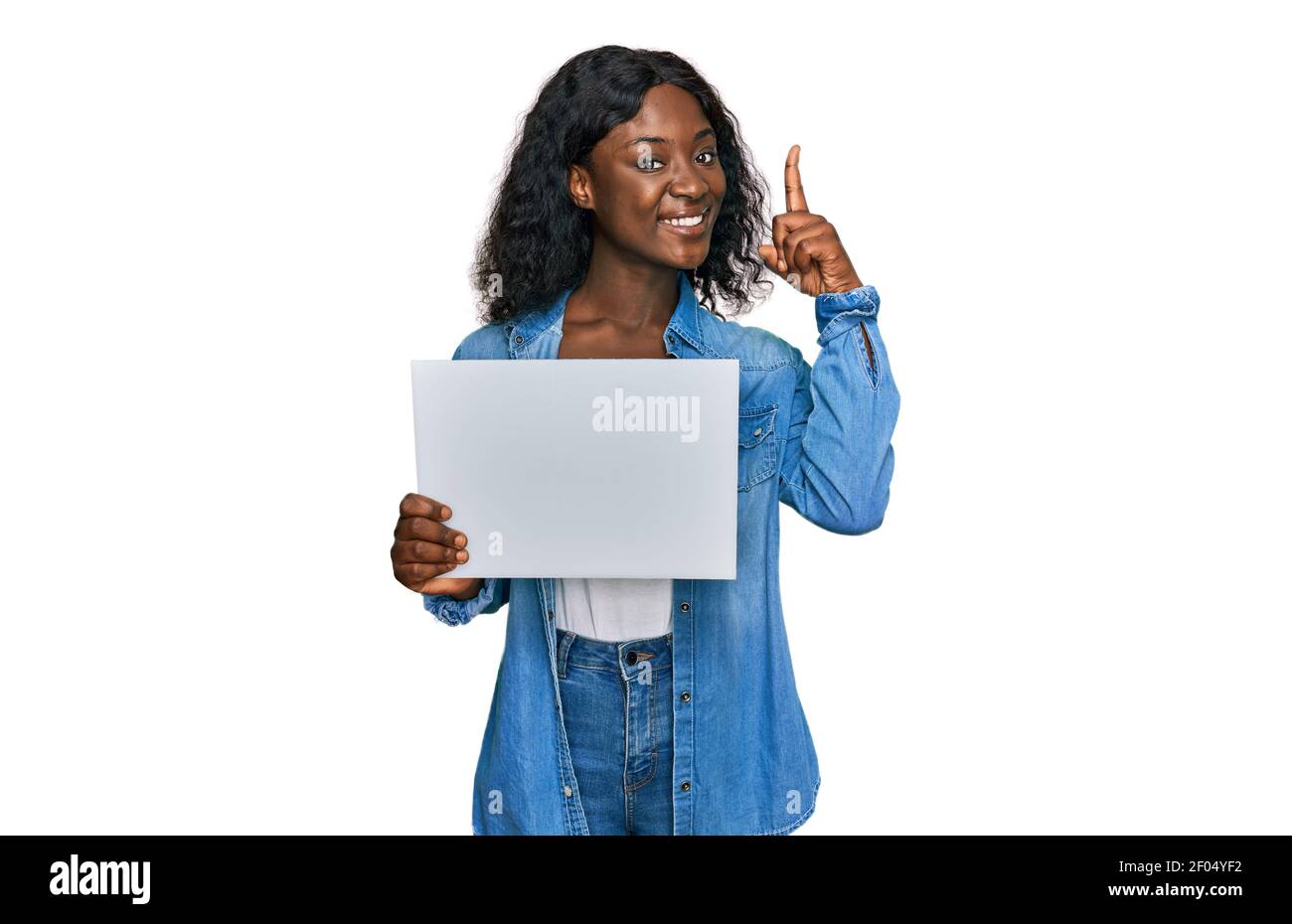 Beautiful african young woman holding blank empty banner surprised with ...