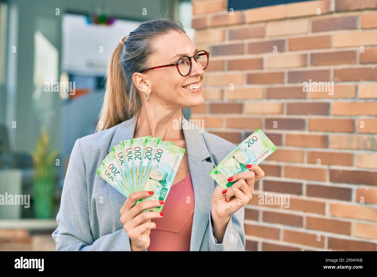 Young blonde businesswoman smiling happy holding russian 200 ruble ...