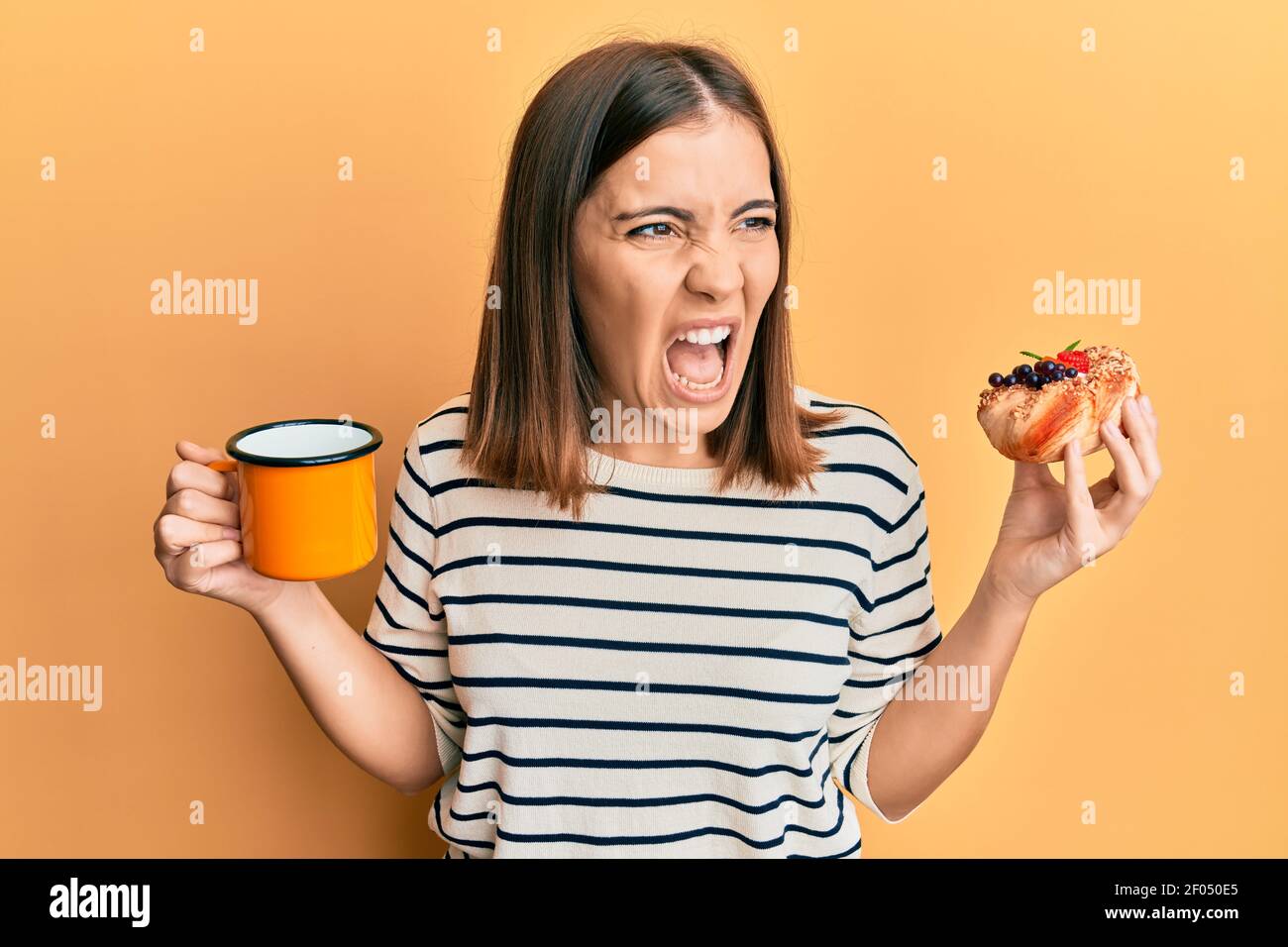 Young beautiful woman drinking coffee and eating pastry angry and mad ...