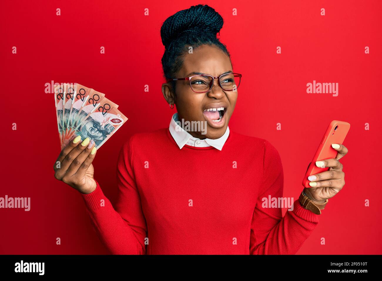 Young african american woman using smartphone holding australian dollar ...