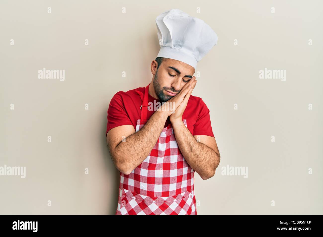 Young hispanic man wearing baker uniform sleeping tired dreaming and ...
