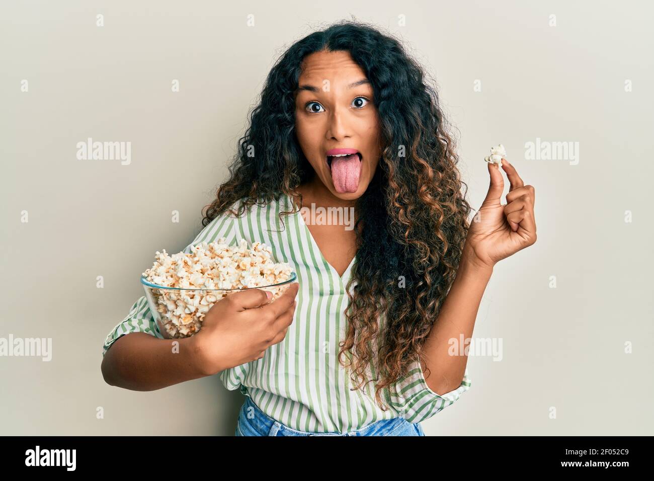 Young latin woman eating popcorn sticking tongue out happy with funny ...
