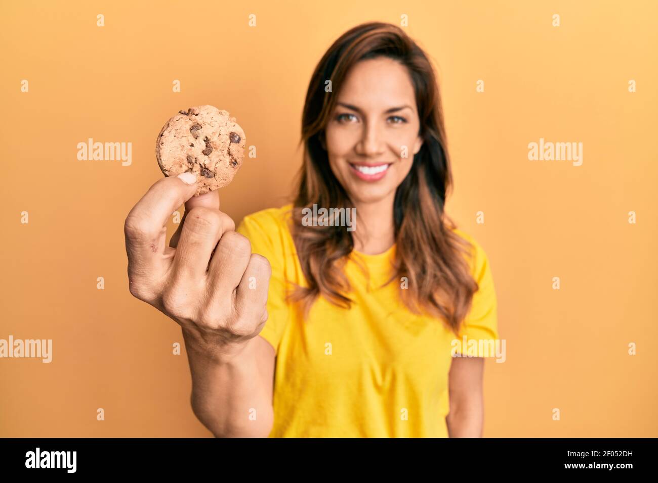 Young latin woman holding cookie looking positive and happy standing ...