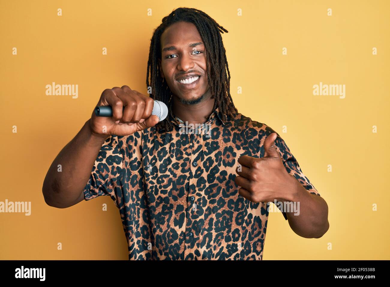African american man with braids singing song using microphone smiling ...