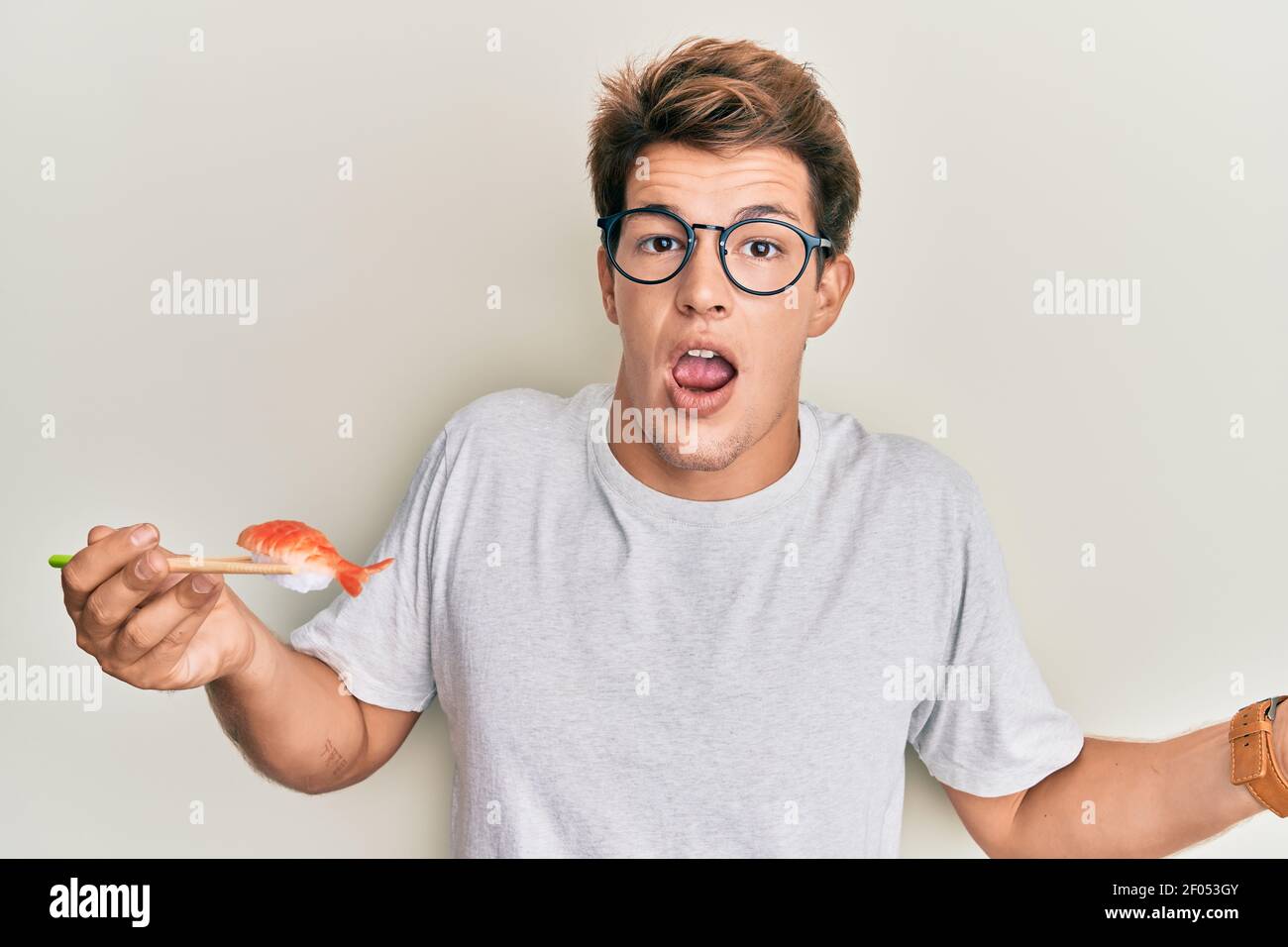 Handsome caucasian man eating prawn sushi using chopsticks celebrating ...