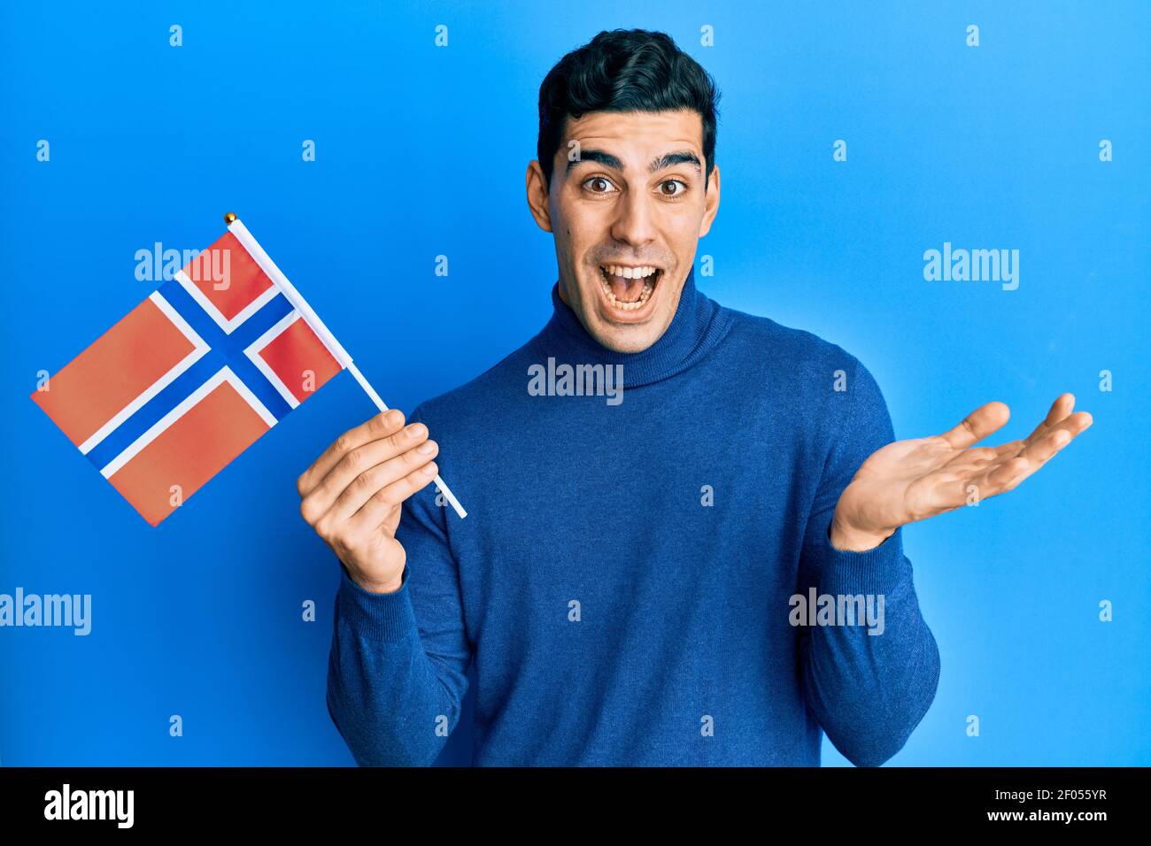 Handsome hispanic man holding norway flag celebrating achievement with ...