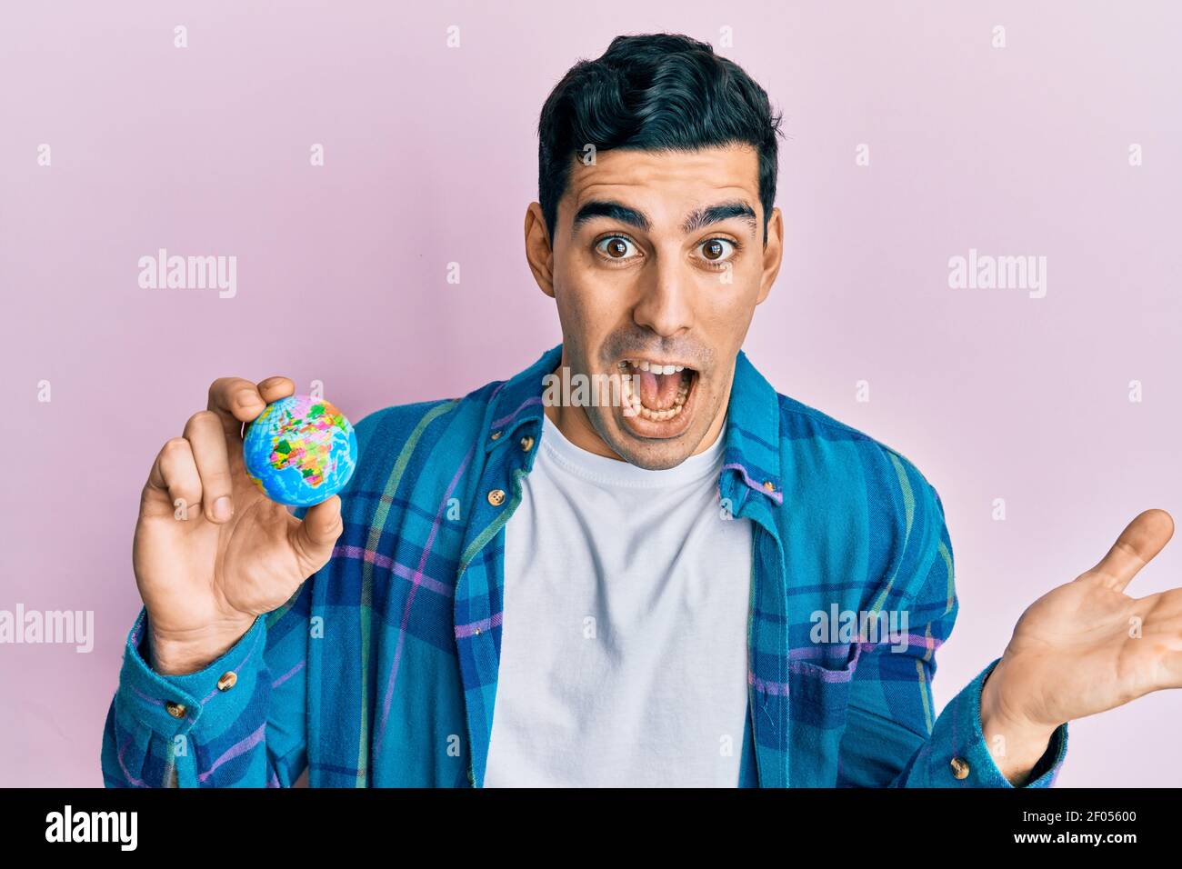 Handsome hispanic man holding small world ball celebrating victory with ...