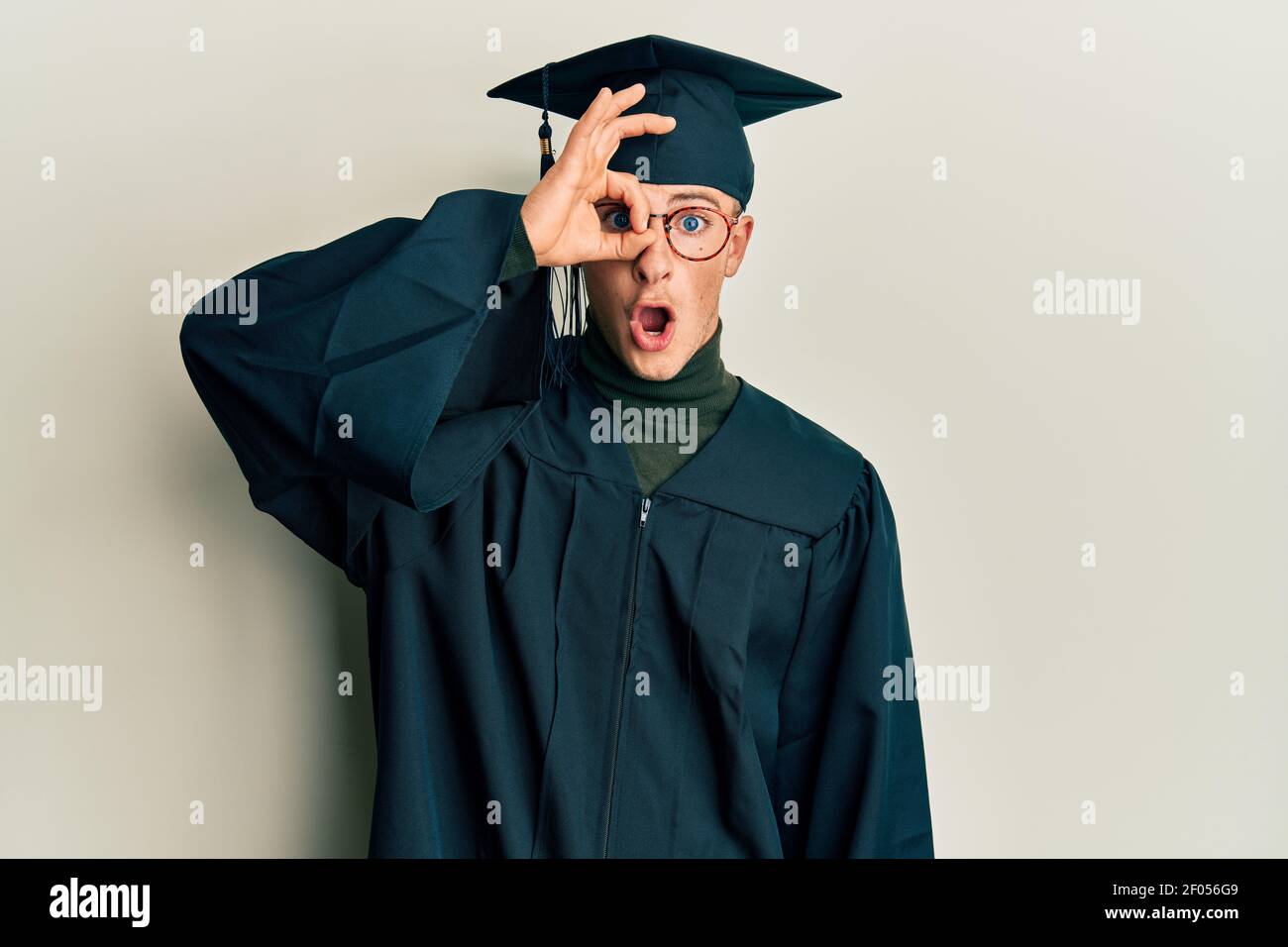 Young caucasian man wearing graduation cap and ceremony robe doing ok ...