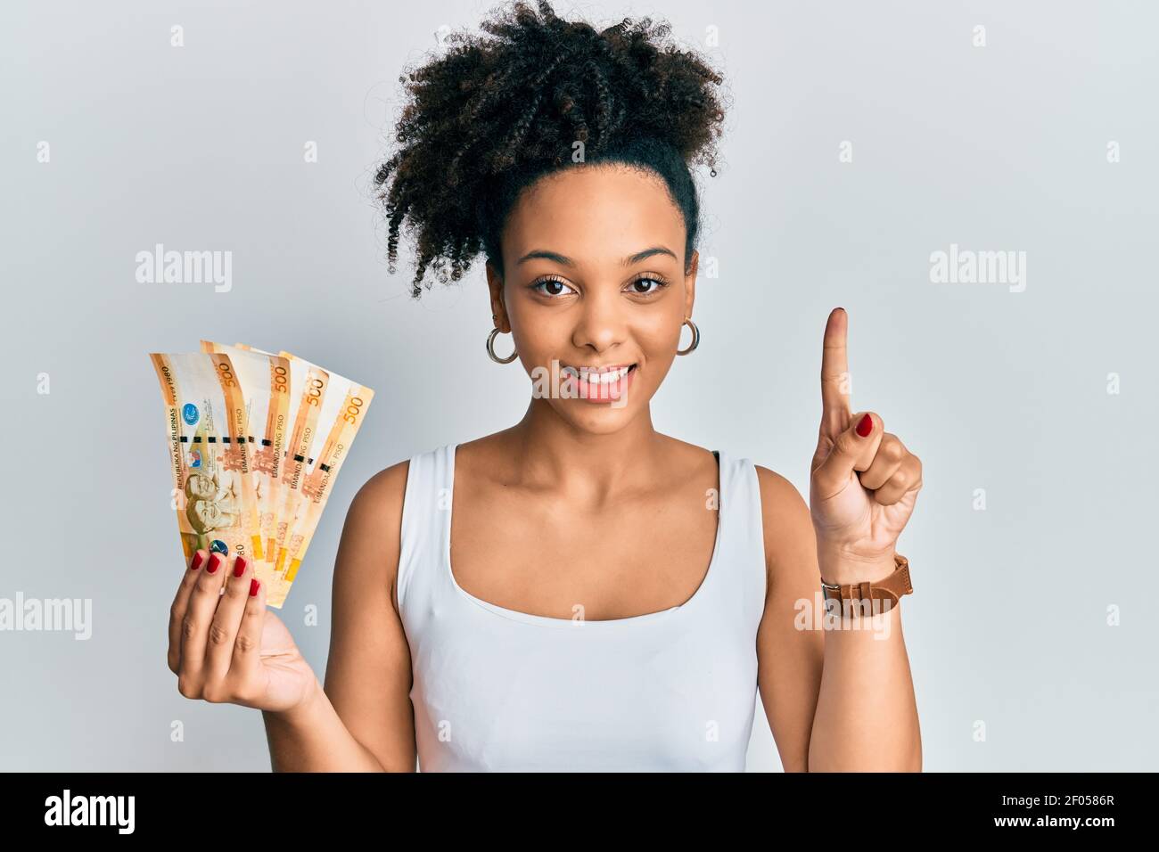 Young african american girl holding philippine peso banknotes smiling ...