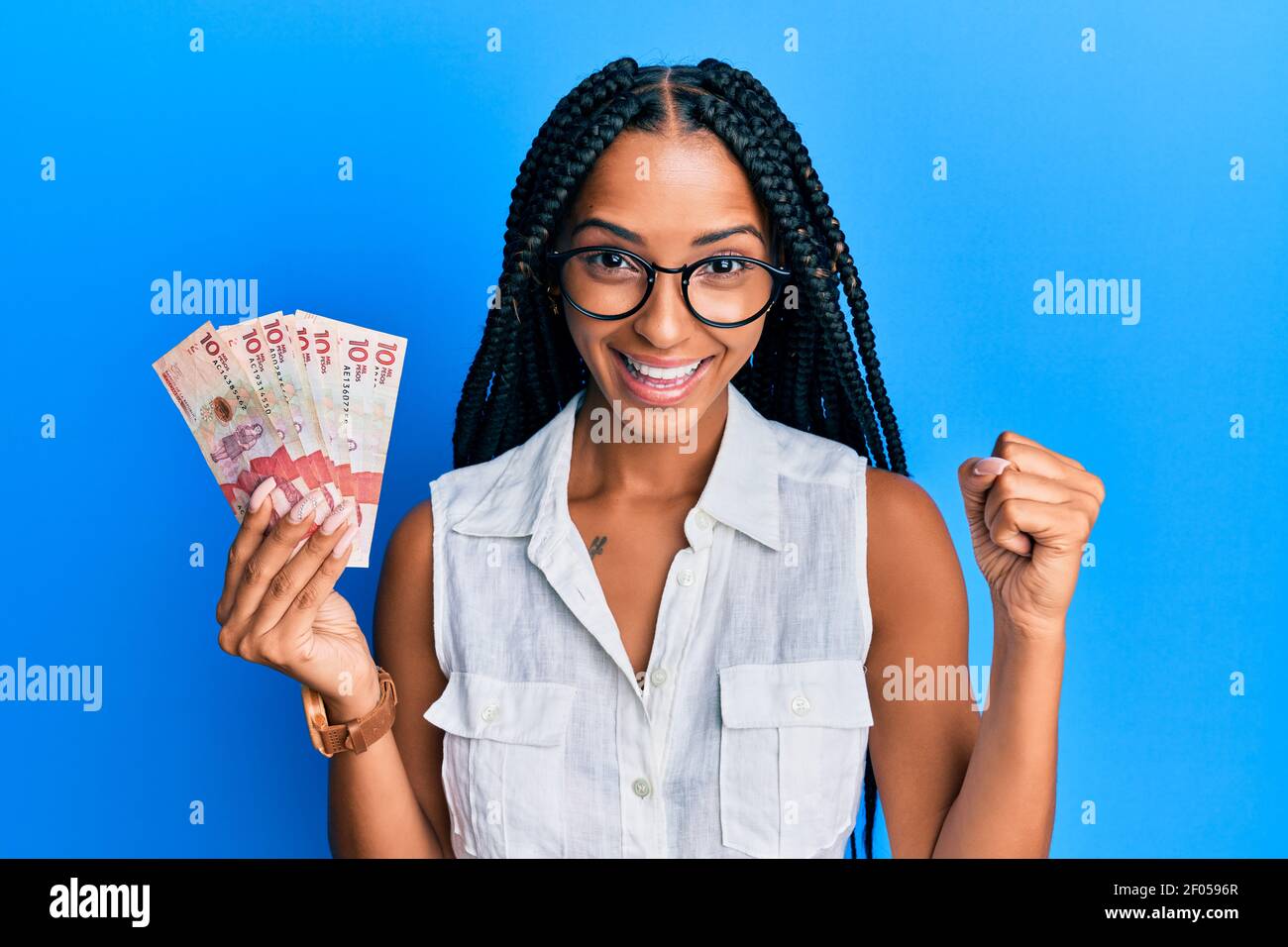 Beautiful hispanic woman holding 10 colombian pesos banknotes screaming ...