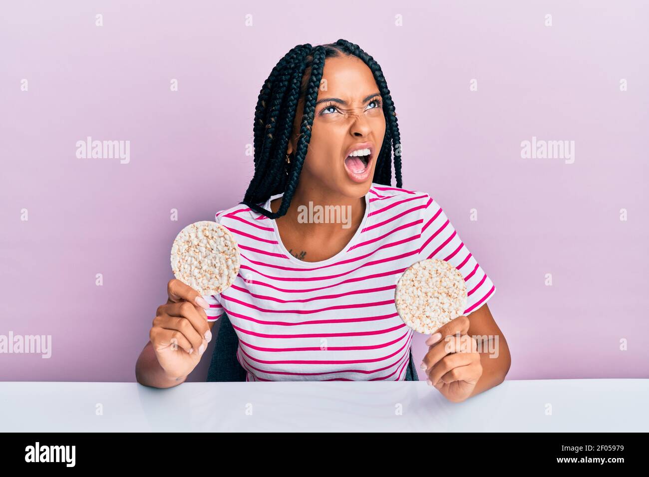 Beautiful hispanic woman eating healthy rice crackers angry and mad ...