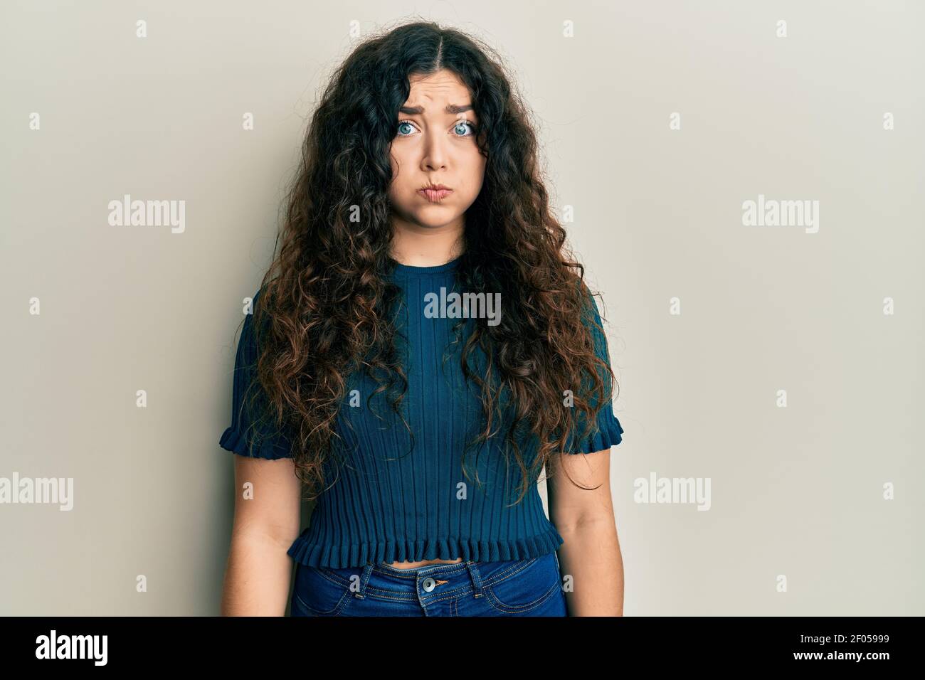 Young brunette woman with curly hair wearing casual clothes puffing ...