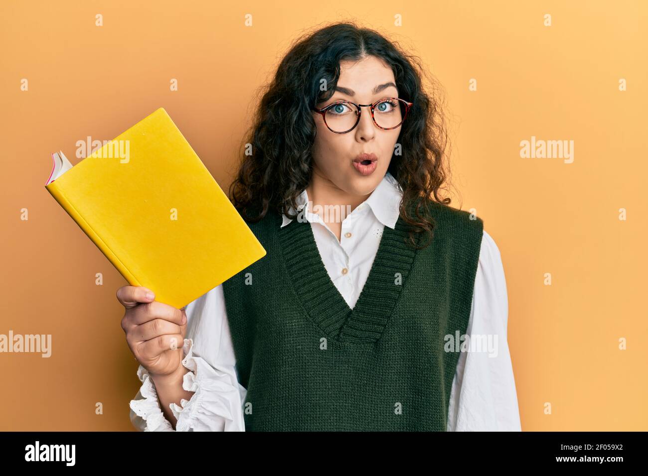 Young brunette woman with curly hair reading a book wearing glasses ...