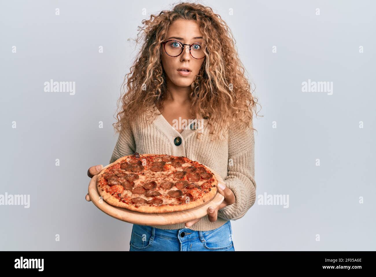Beautiful caucasian teenager girl eating tasty pepperoni pizza clueless ...