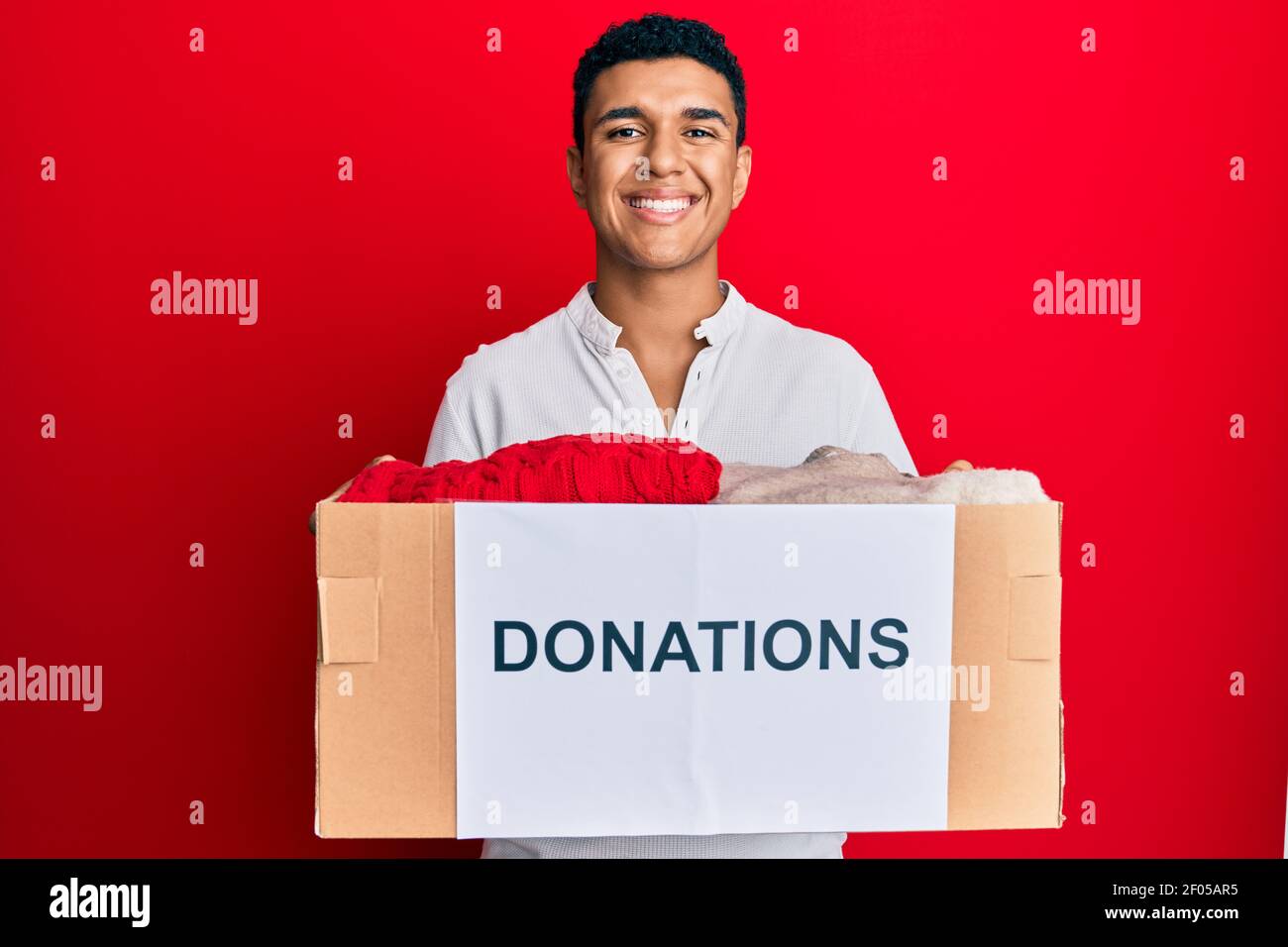 Young arab man holding donation box with clothes smiling with a happy ...