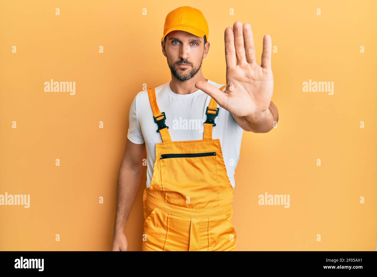 Young handsome man wearing handyman uniform over yellow background ...