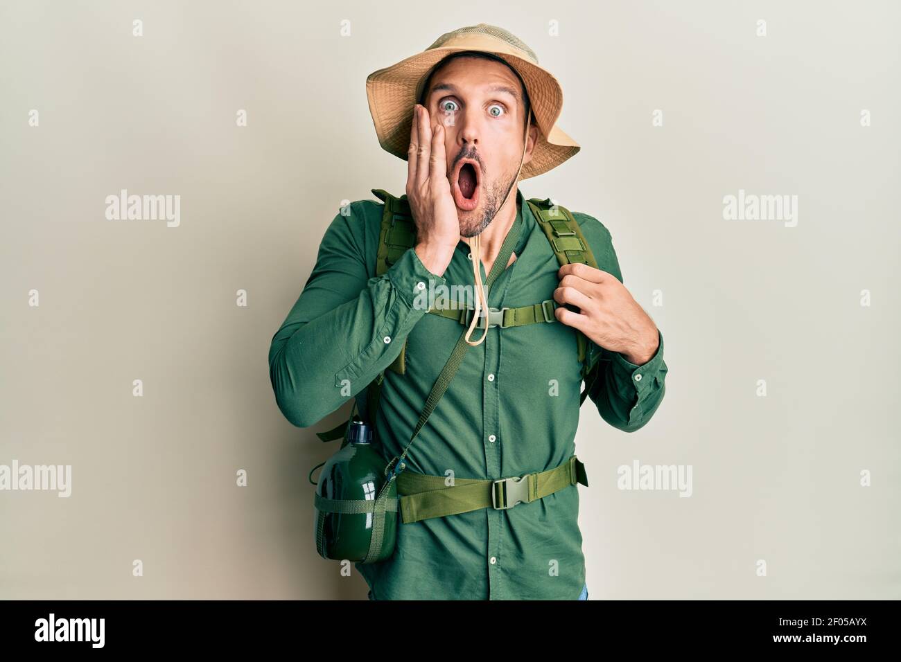 Handsome man with beard wearing explorer hat and backpack afraid and ...