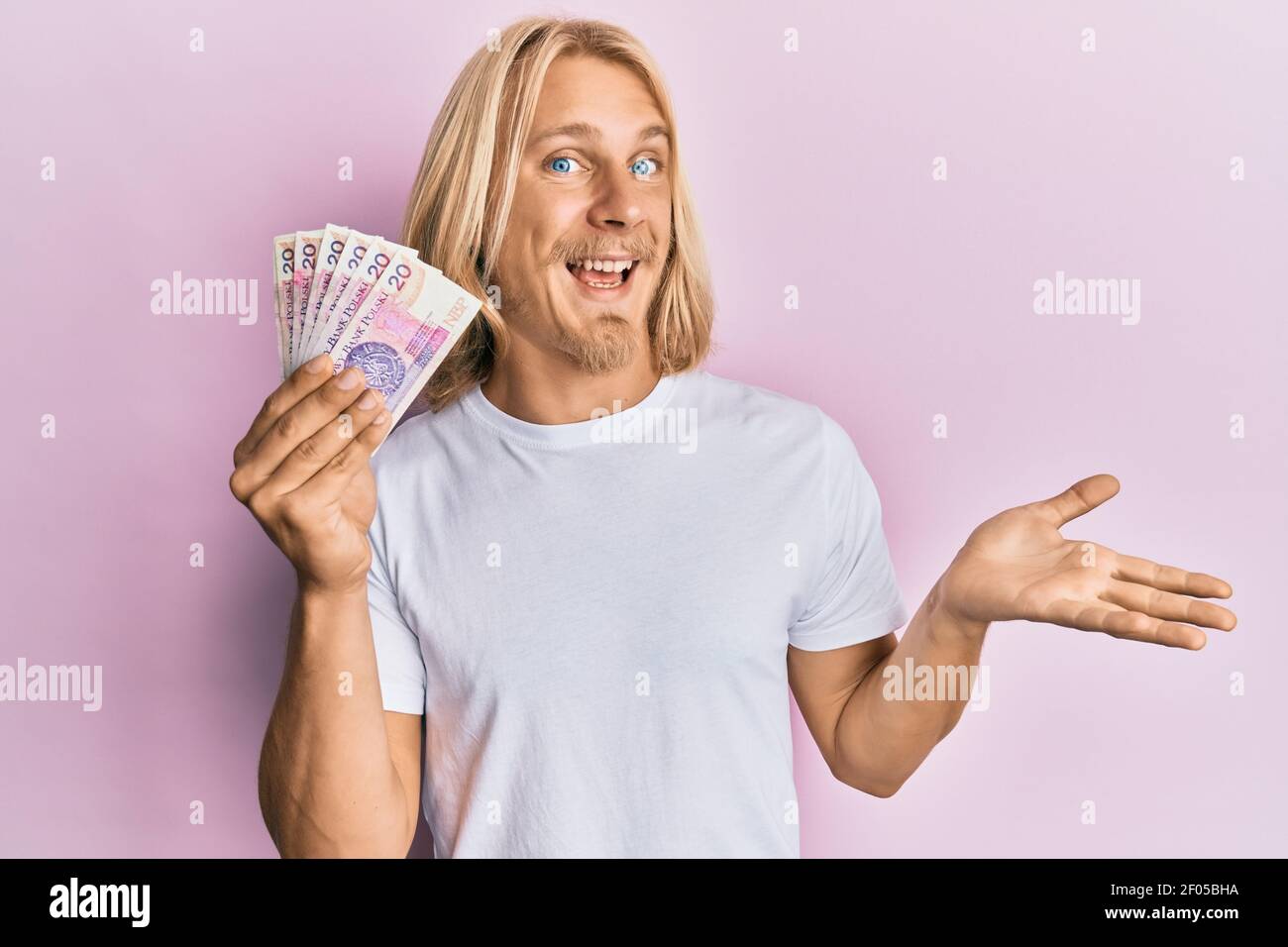 Caucasian young man with long hair holding 20 polish zloty banknotes ...