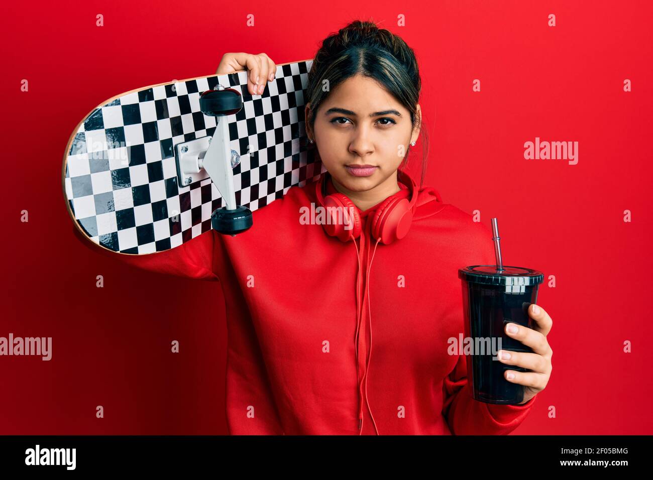 Young latin woman holding skate drinking soda skeptic and nervous ...