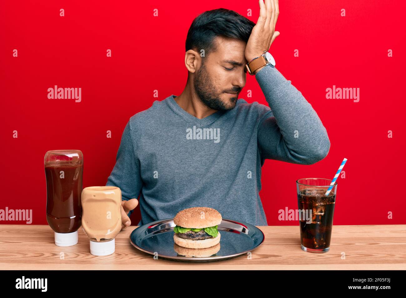 Handsome hispanic man eating a tasty classic burger and soda surprised ...