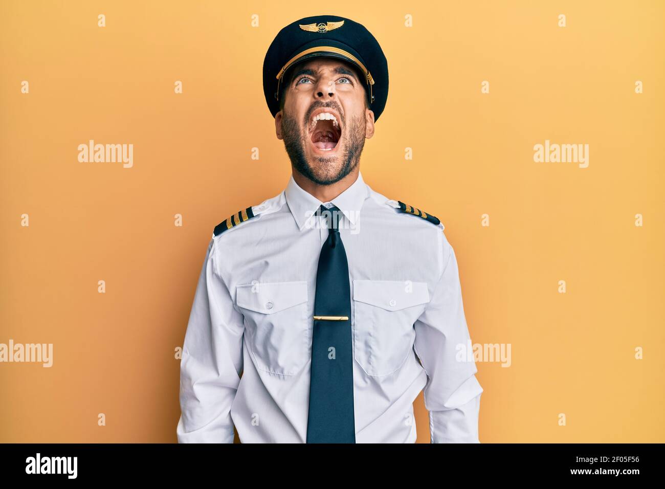 Handsome hispanic man wearing airplane pilot uniform angry and mad ...