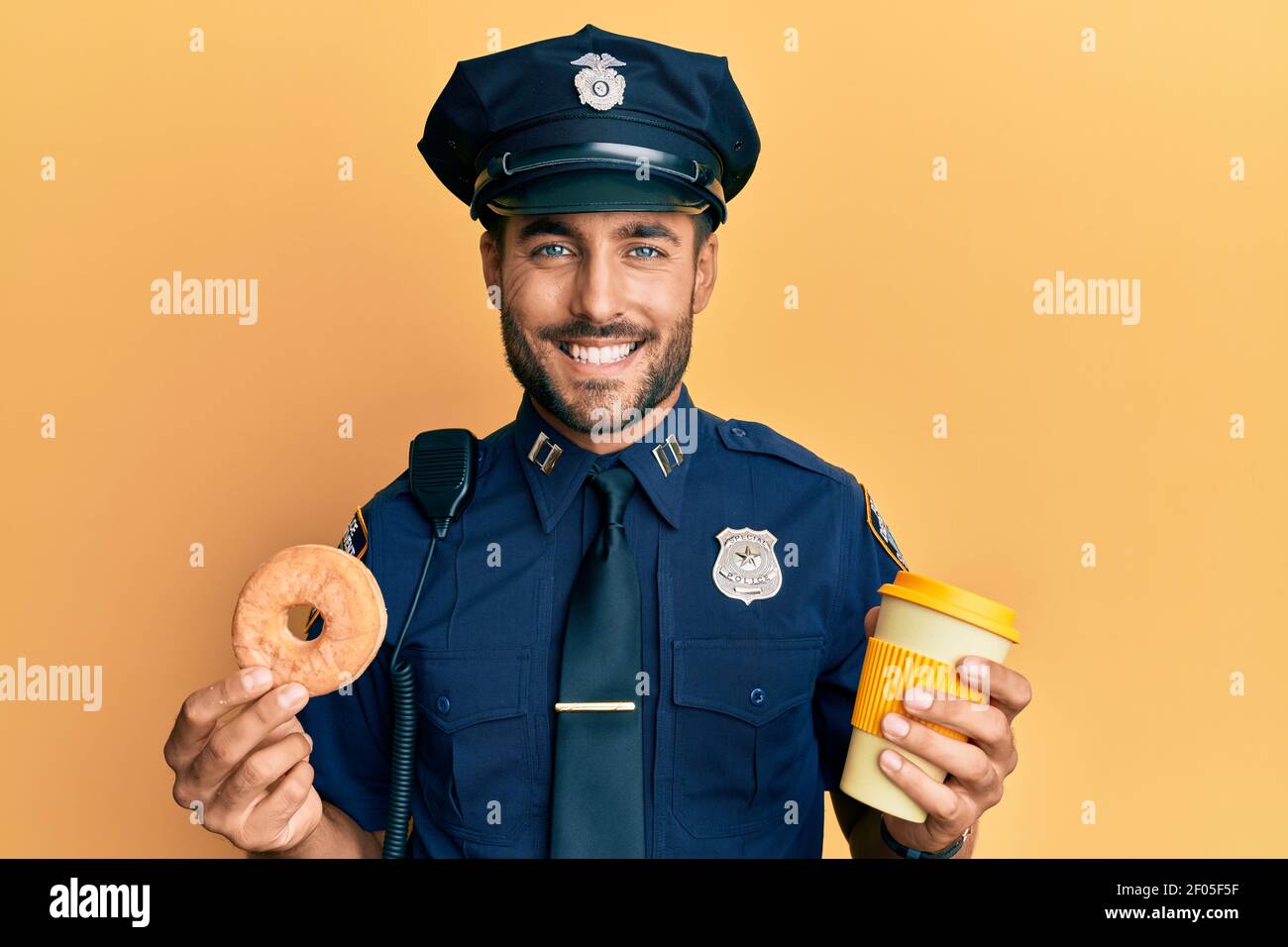 Handsome hispanic police man eating donut and drinking coffee smiling ...