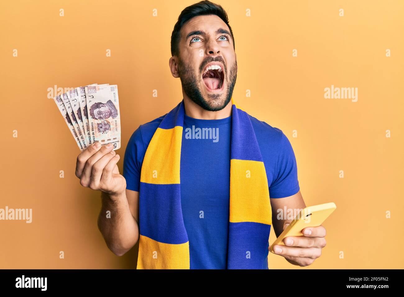 Young hispanic man football supporter using smartphone holding mexican ...