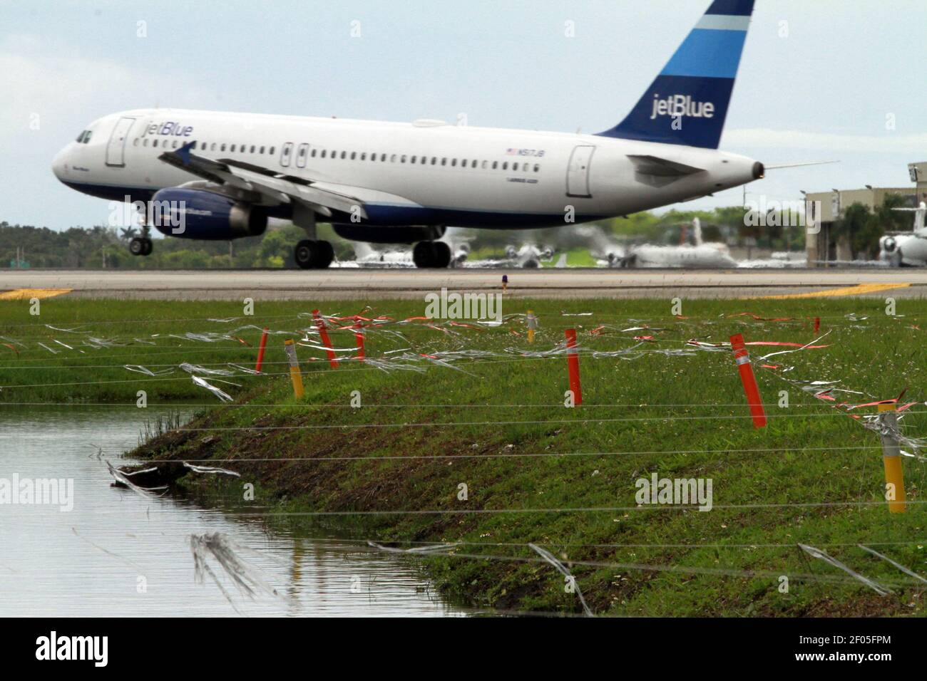 A Jet Blue airplane lands near a water retention basin with ...