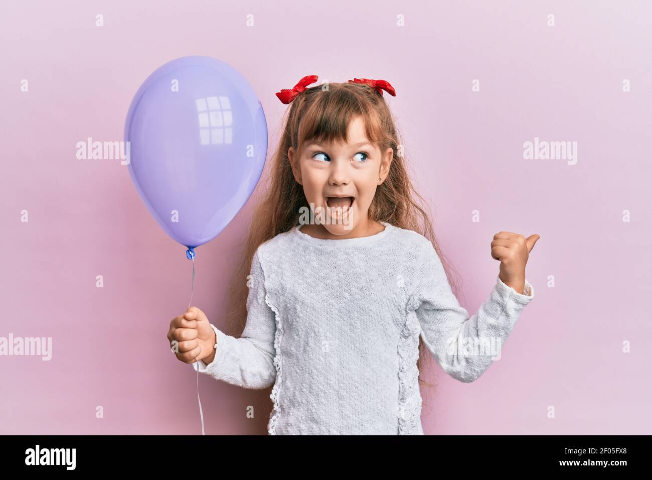 Little caucasian girl kid holding purple balloon pointing thumb up to ...