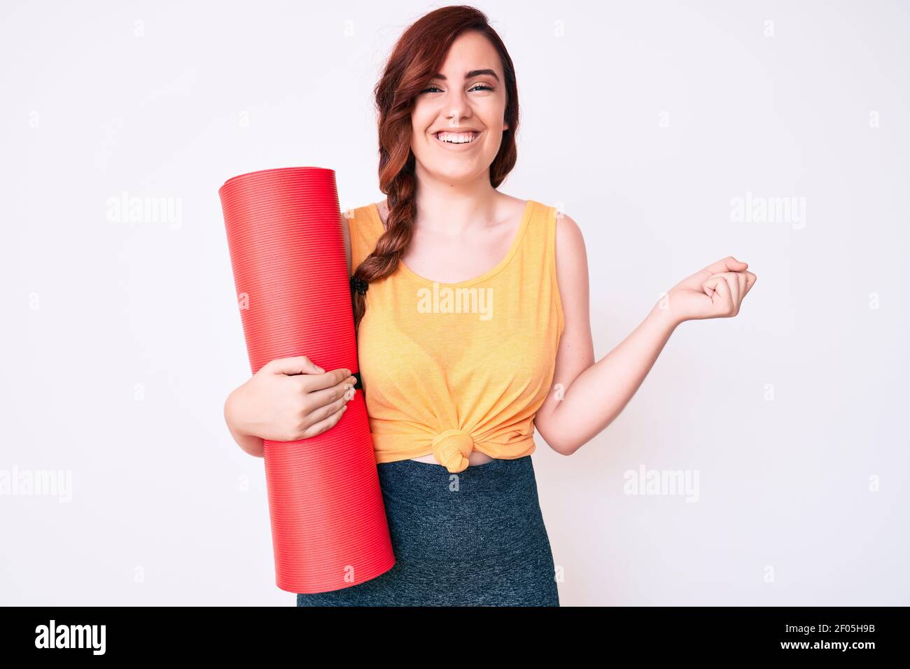 Young beautiful woman holding yoga mat screaming proud, celebrating ...