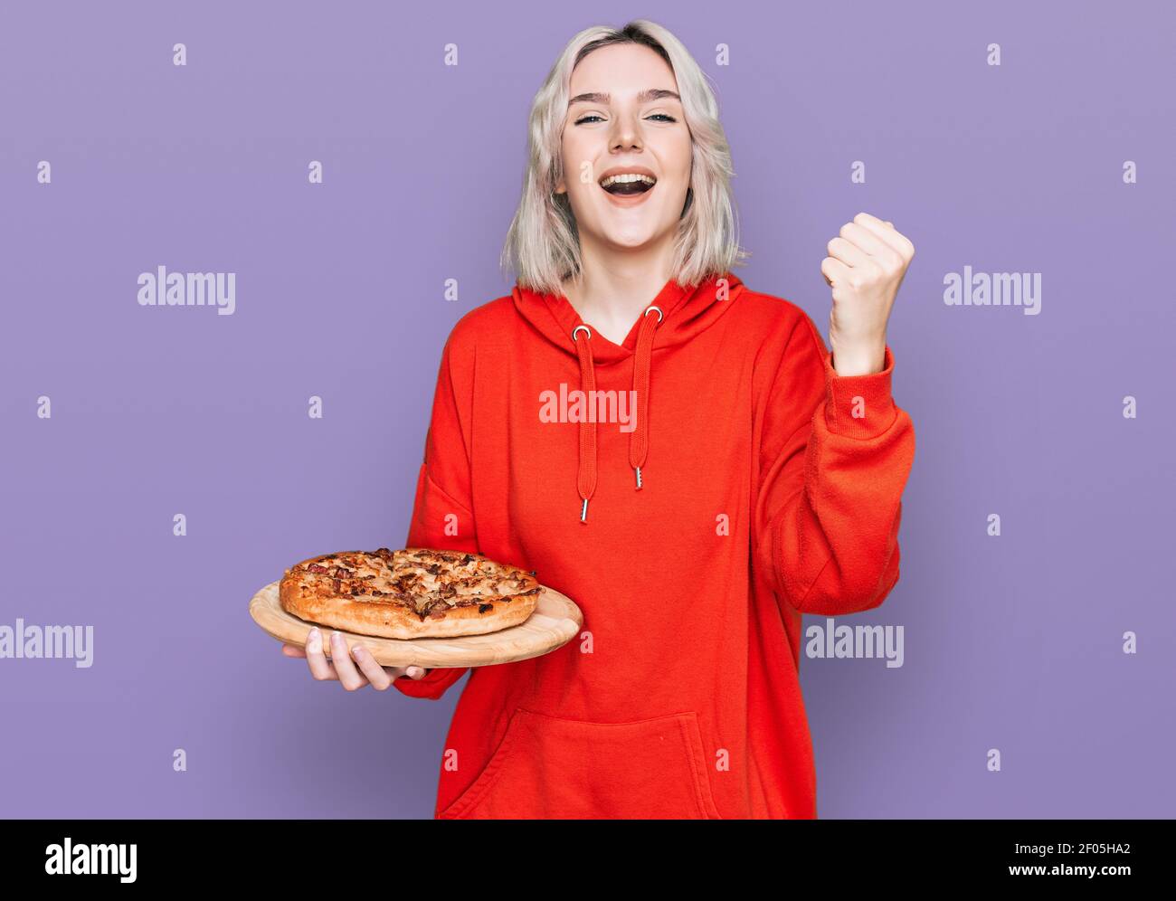 Young blonde girl holding italian pizza screaming proud, celebrating ...