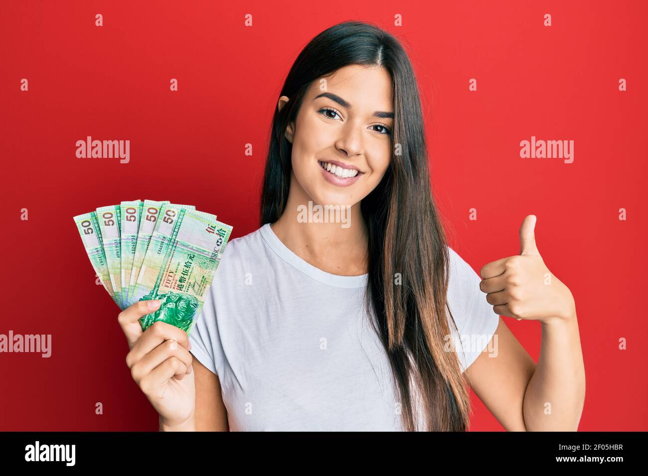 Young brunette woman holding hong kong 50 dollars banknotes smiling ...