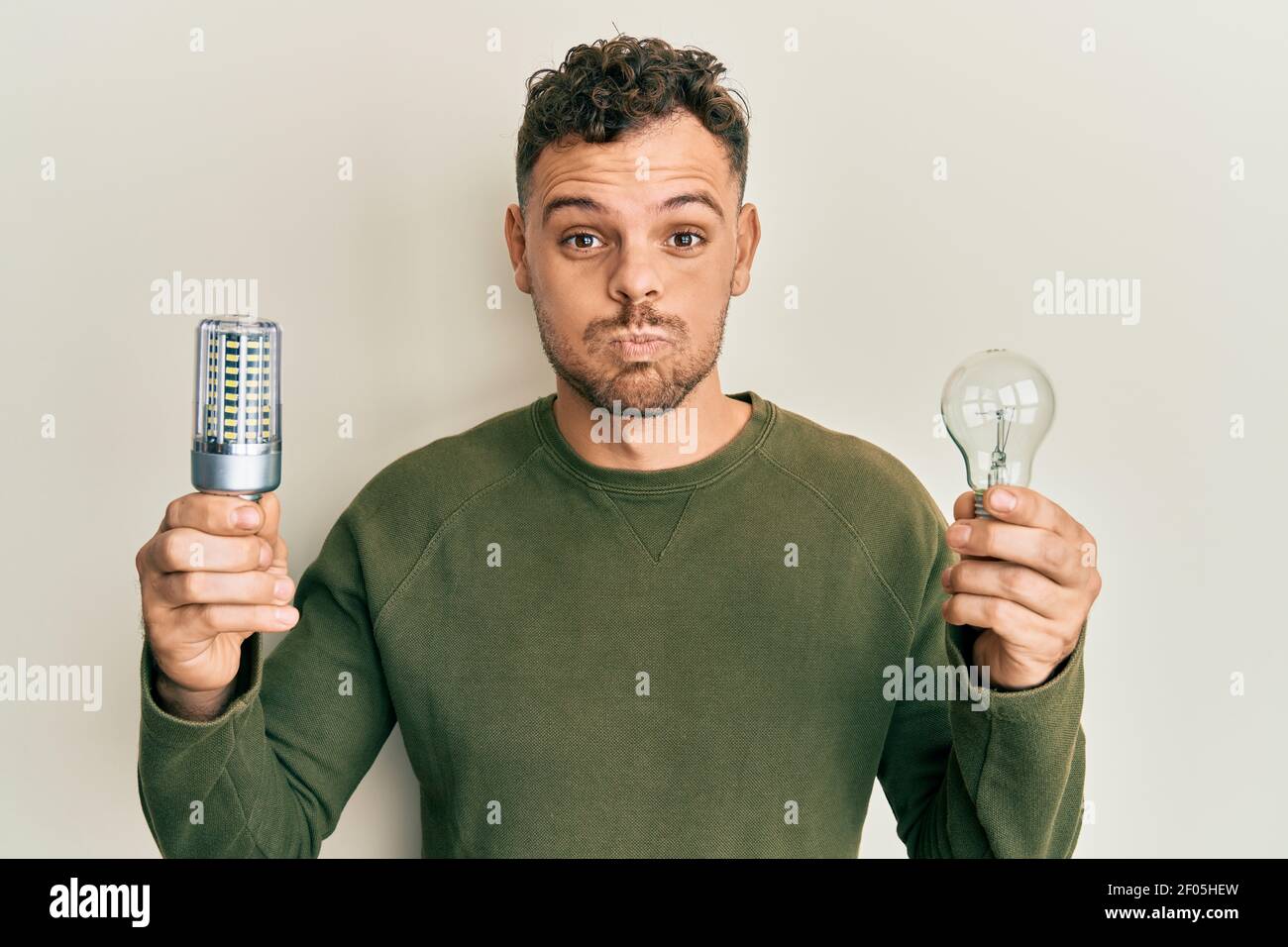 Young hispanic man holding lightbulb for inspiration and idea puffing ...