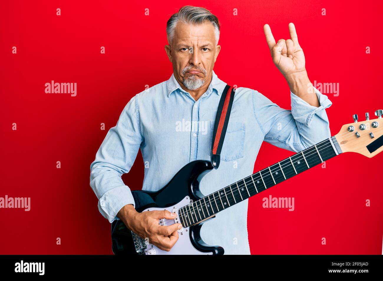 Middle age grey-haired man playing electric guitar doing rock sign ...