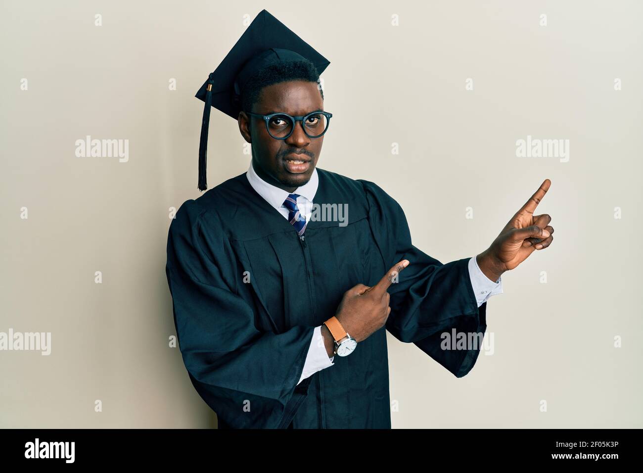 Handsome black man wearing graduation cap and ceremony robe pointing ...