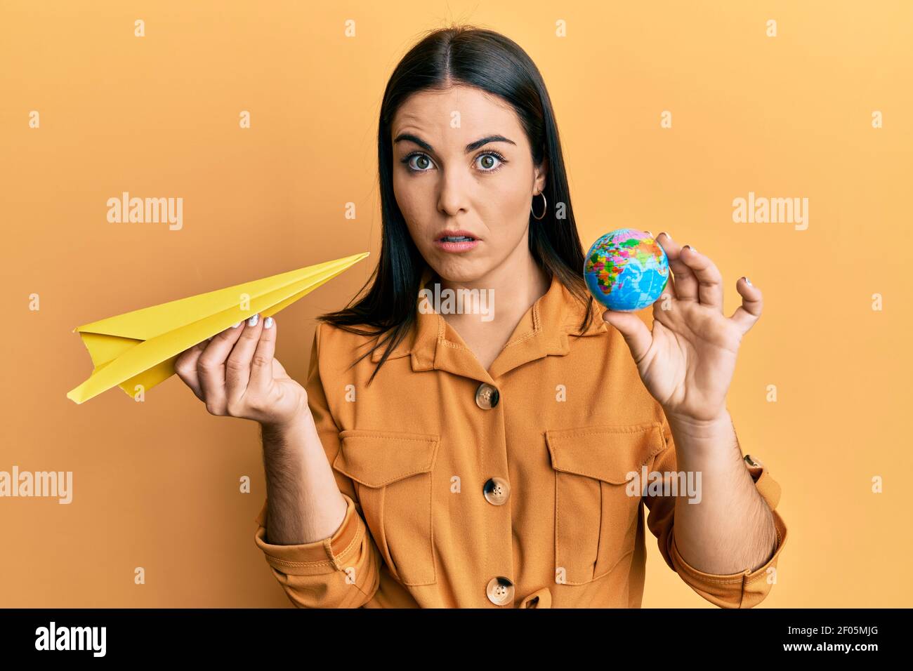 Young brunette woman holding paper plane and world ball clueless and ...