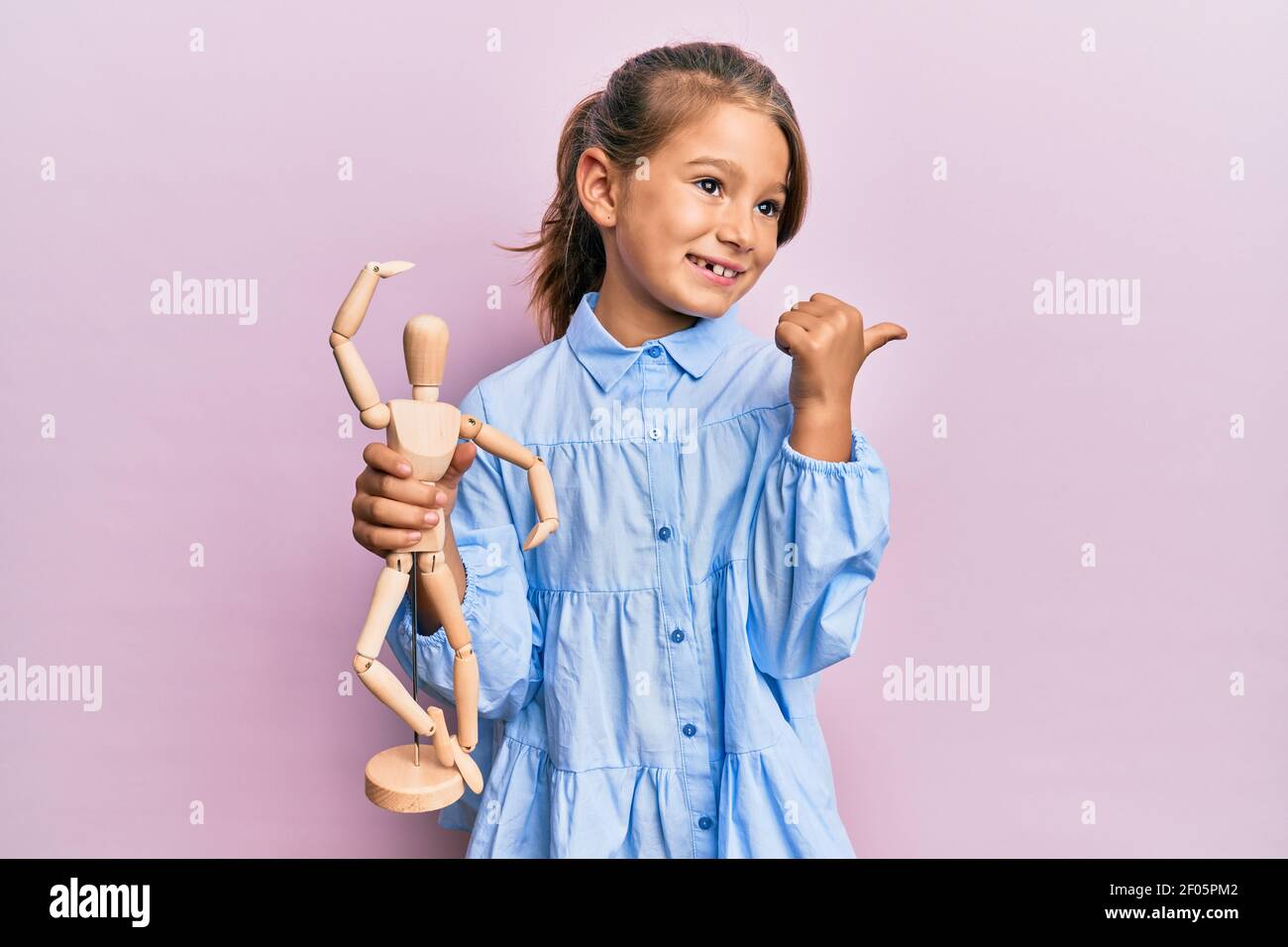 Little beautiful girl holding small wooden manikin pointing thumb up to ...