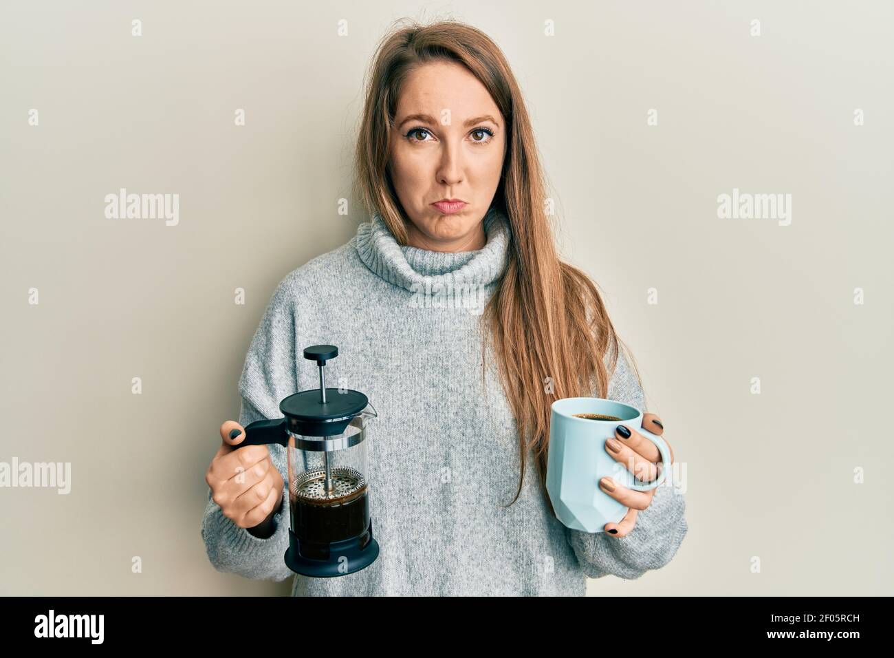 Young blonde woman drinking a cup of italian coffee depressed and worry ...