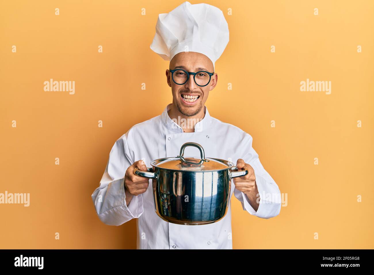 Bald man with beard wearing professional cook holding cooking pot ...