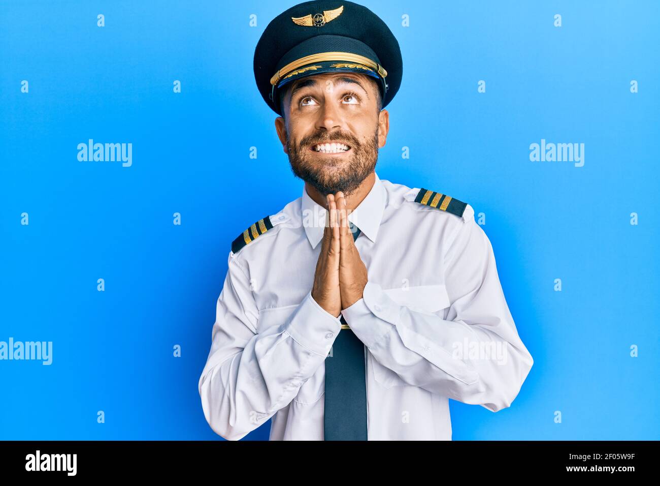 Handsome man with beard wearing airplane pilot uniform begging and ...