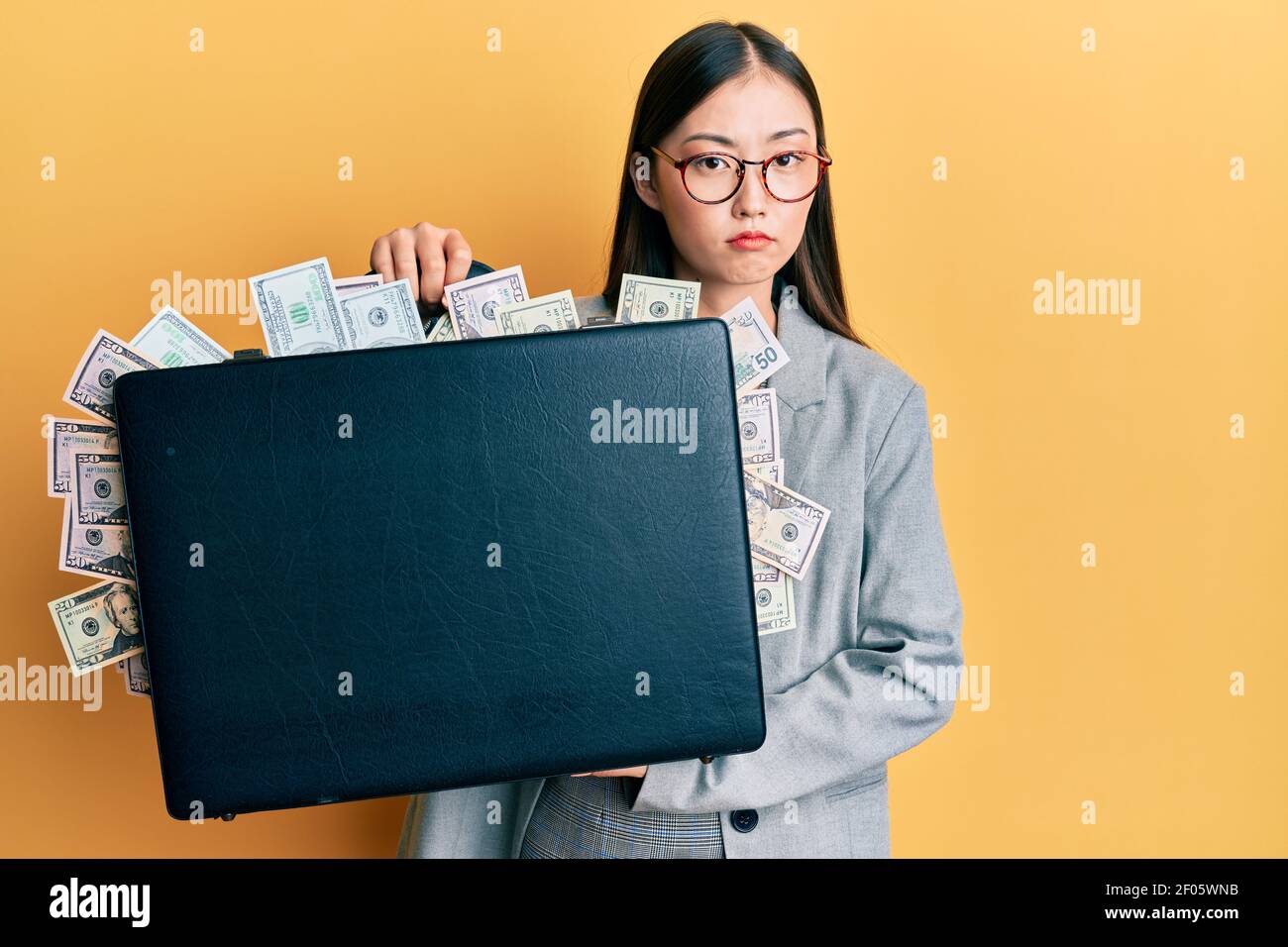 Young chinese woman holding briefcase full of dollars depressed and ...