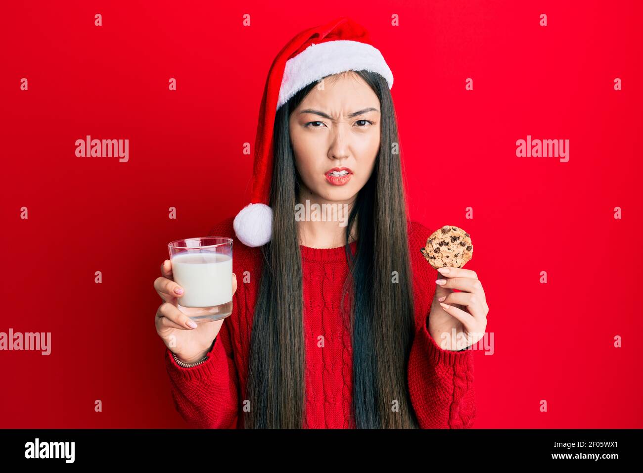 Young chinese woman wearing christmas hat holding cookies and milk ...