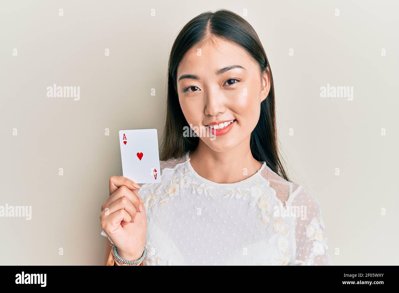 Young chinese woman holding ace poker card looking positive and happy ...